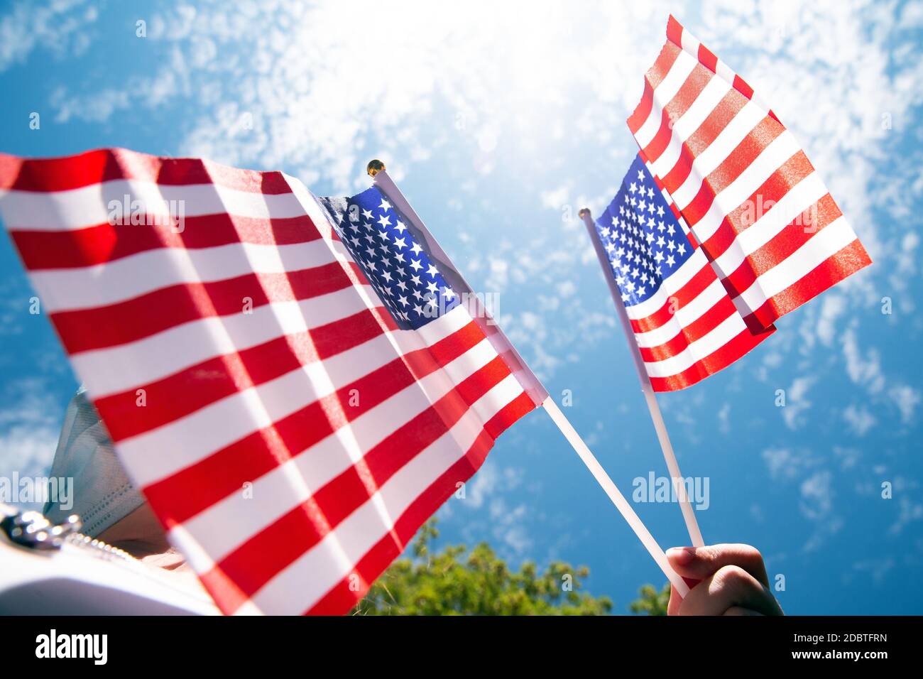 Hand holding two american flags on the blue sky with sunlight ...