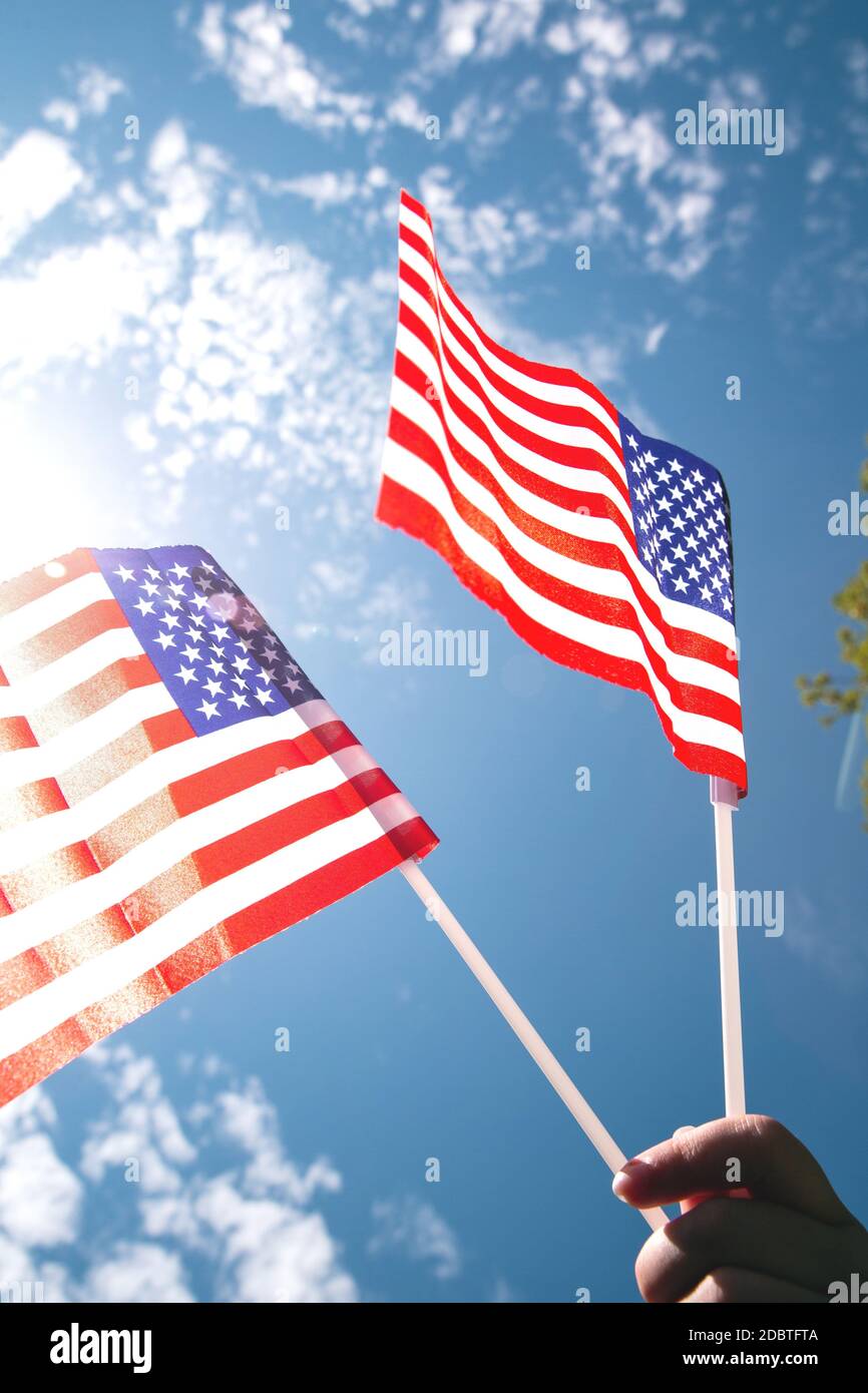 Hand holding two american flags on the blue sky with sunlight ...