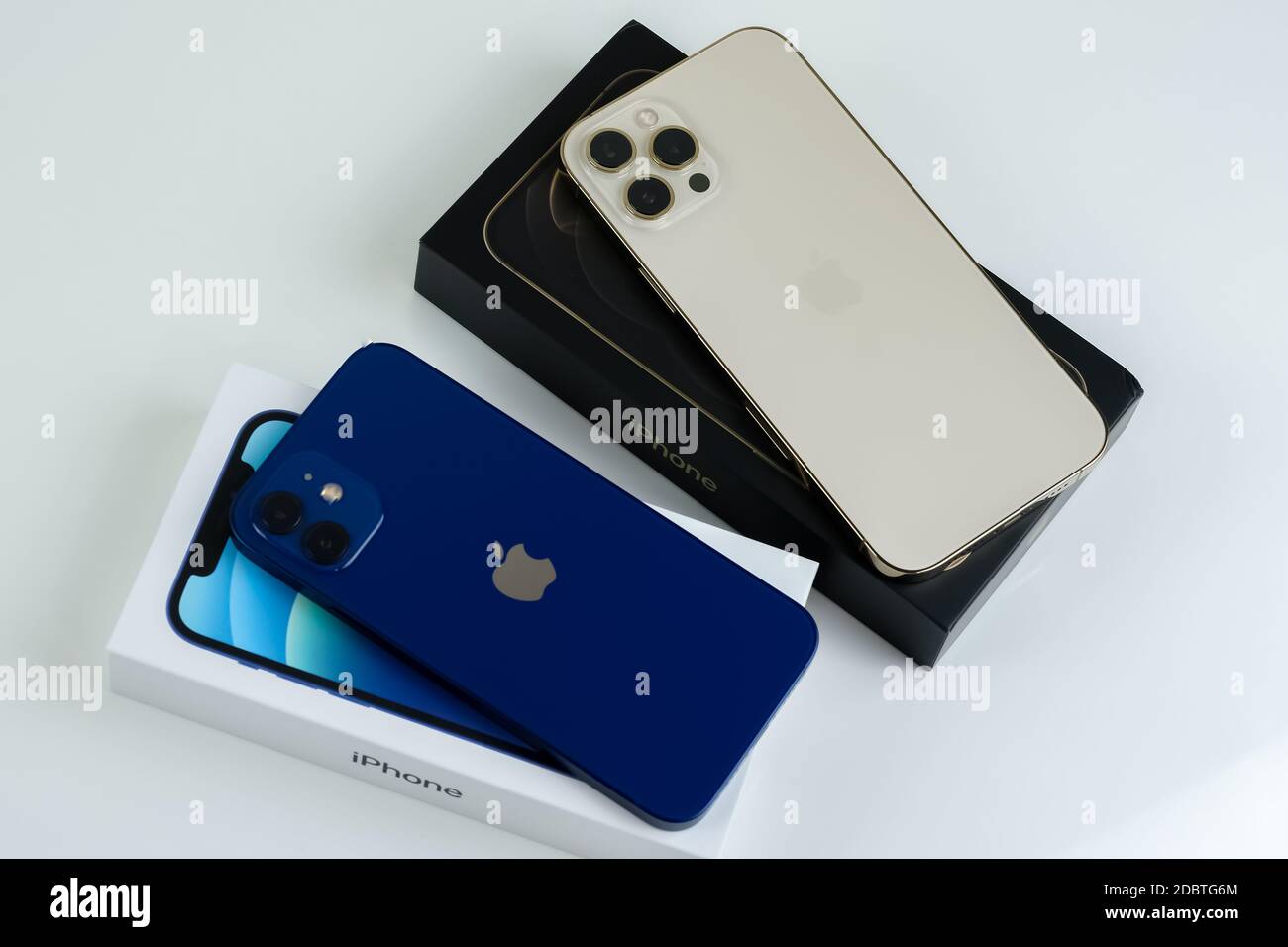 iPhone 12 Pro Max in Gold next to iPhone 12 in Blue on a white desk ...