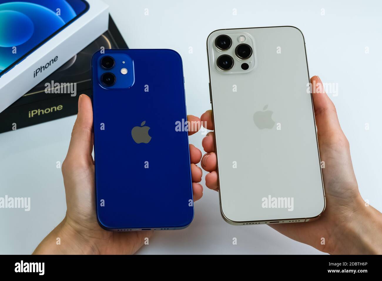 iPhone 12 Pro Max in Gold next to iPhone 12 in Blue on a white desk ...