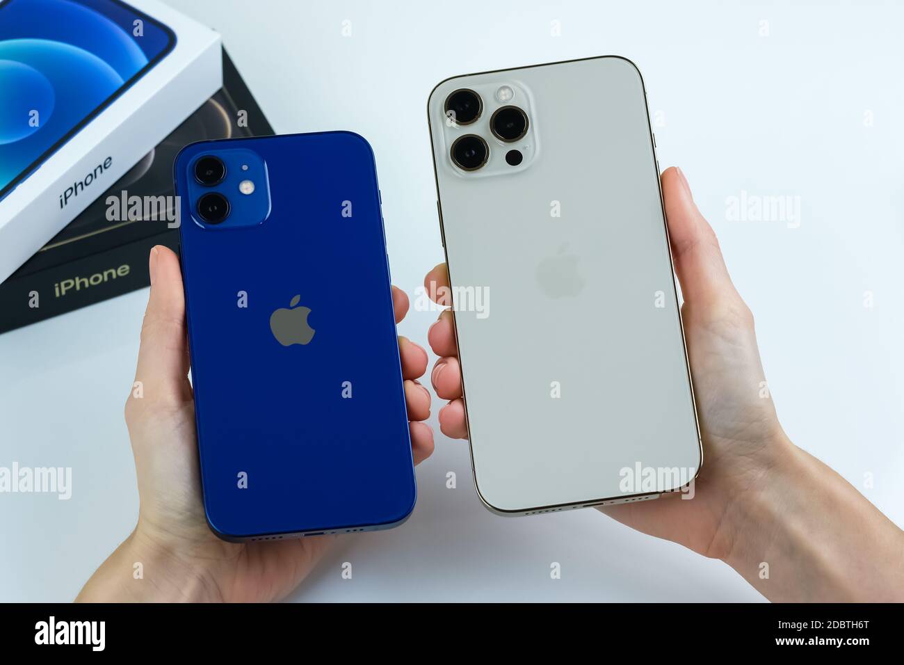 iPhone 12 Pro Max in Gold next to iPhone 12 in Blue on a white desk ...