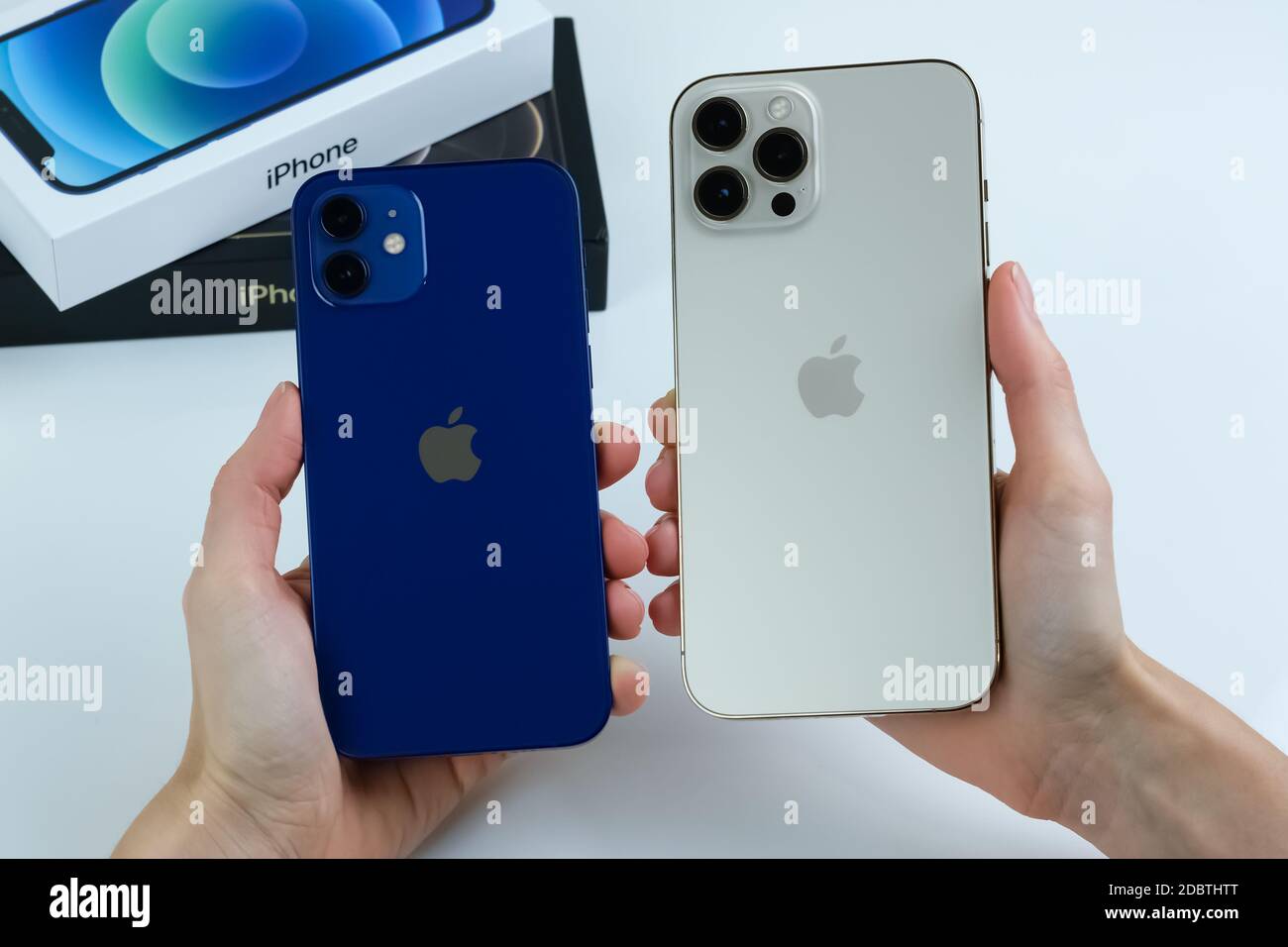 iPhone 12 Pro Max in Gold next to iPhone 12 in Blue on a white desk ...