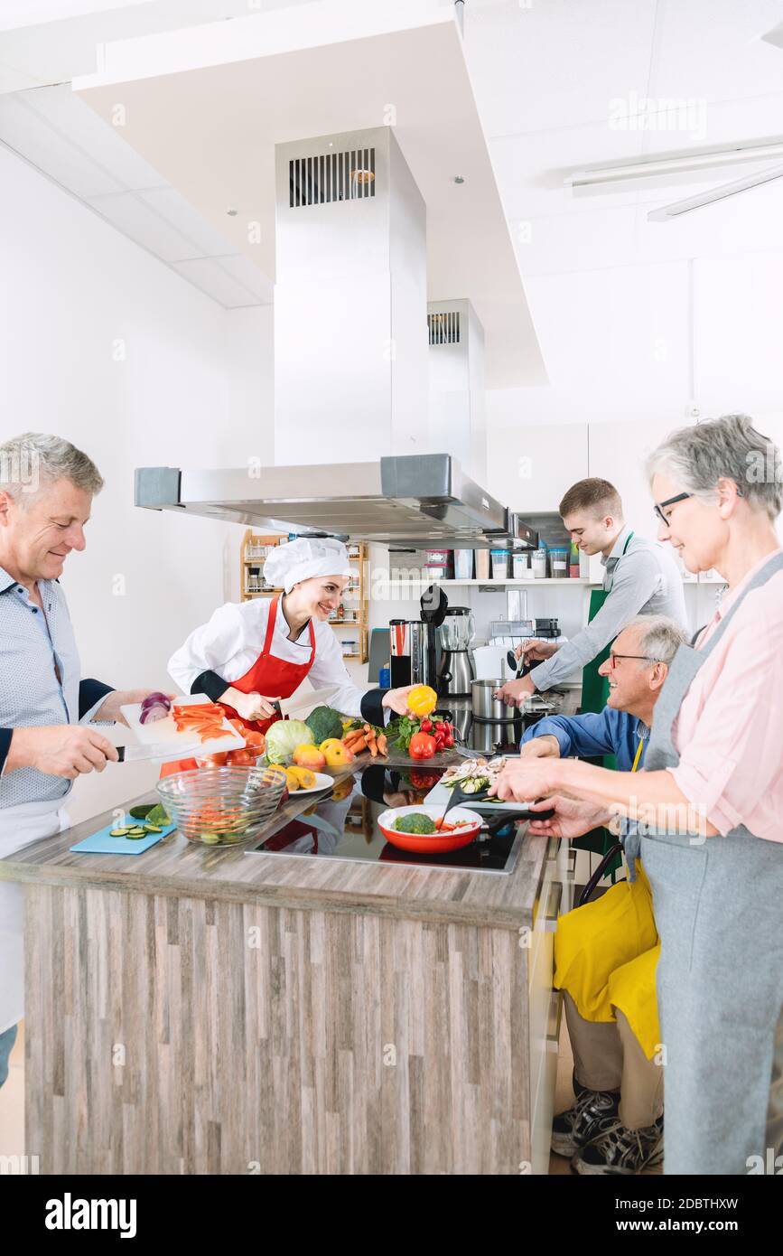 Chef and group of people cutting vegetables and cooking together in ...