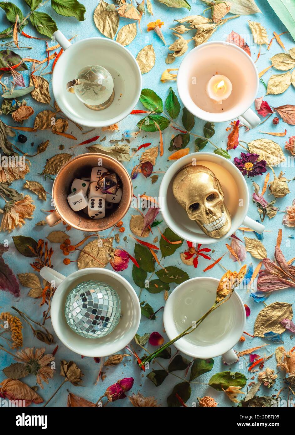 Porcelain cups with trinkets, disco ball, golden scull, petals and ...