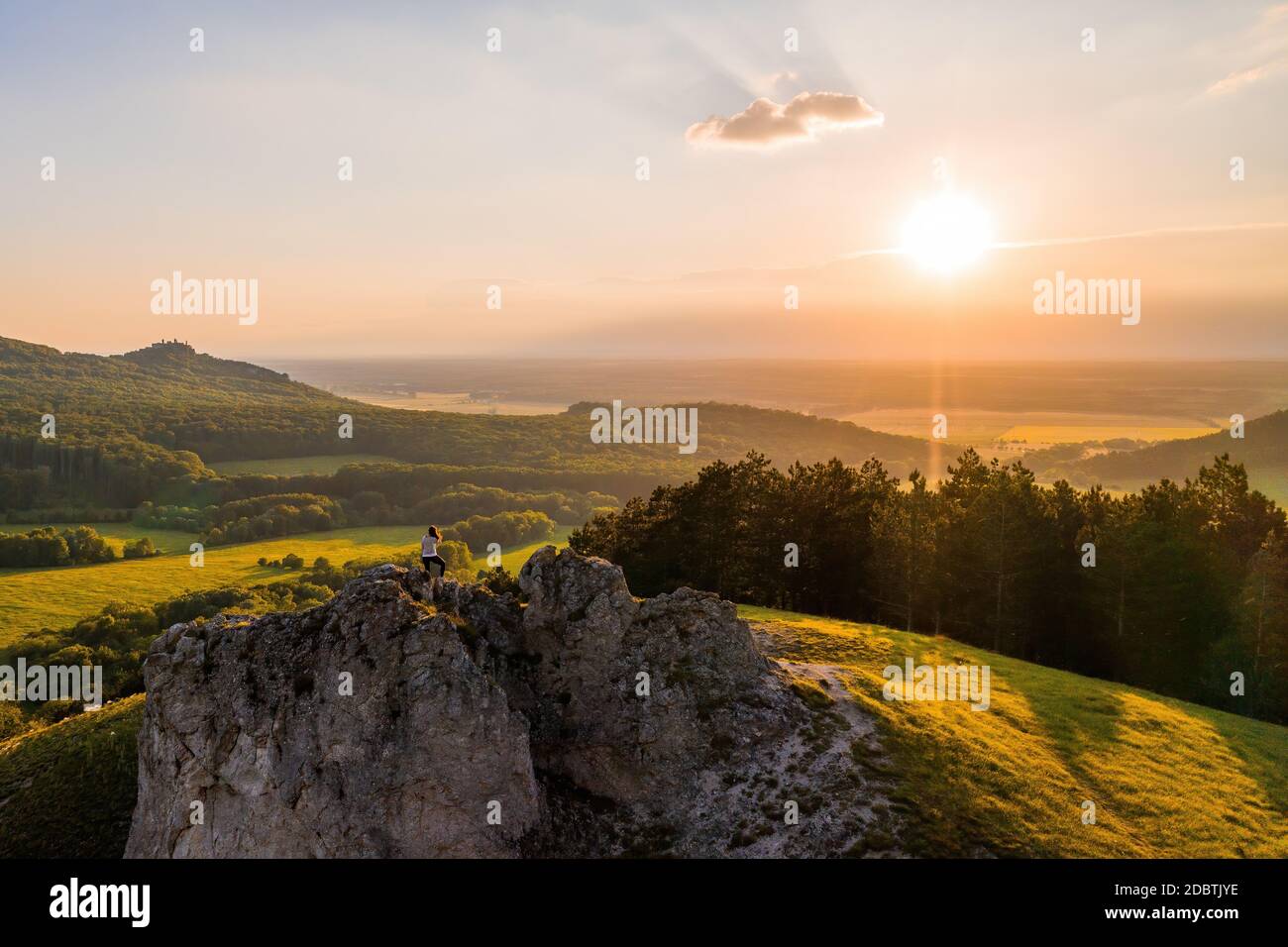 Young woman standing on a rocky horizon and enjoying sunset in summer ...