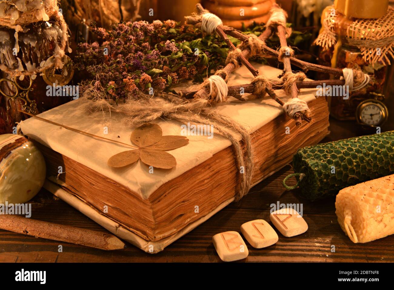 Old book with four-leaf clover, candles, herbs and runes on witch table ...