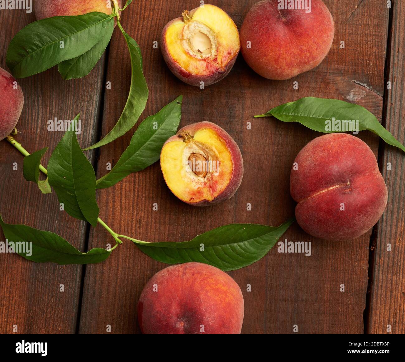 ripe red peaches and green leaves on a brown wooden table, top view ...