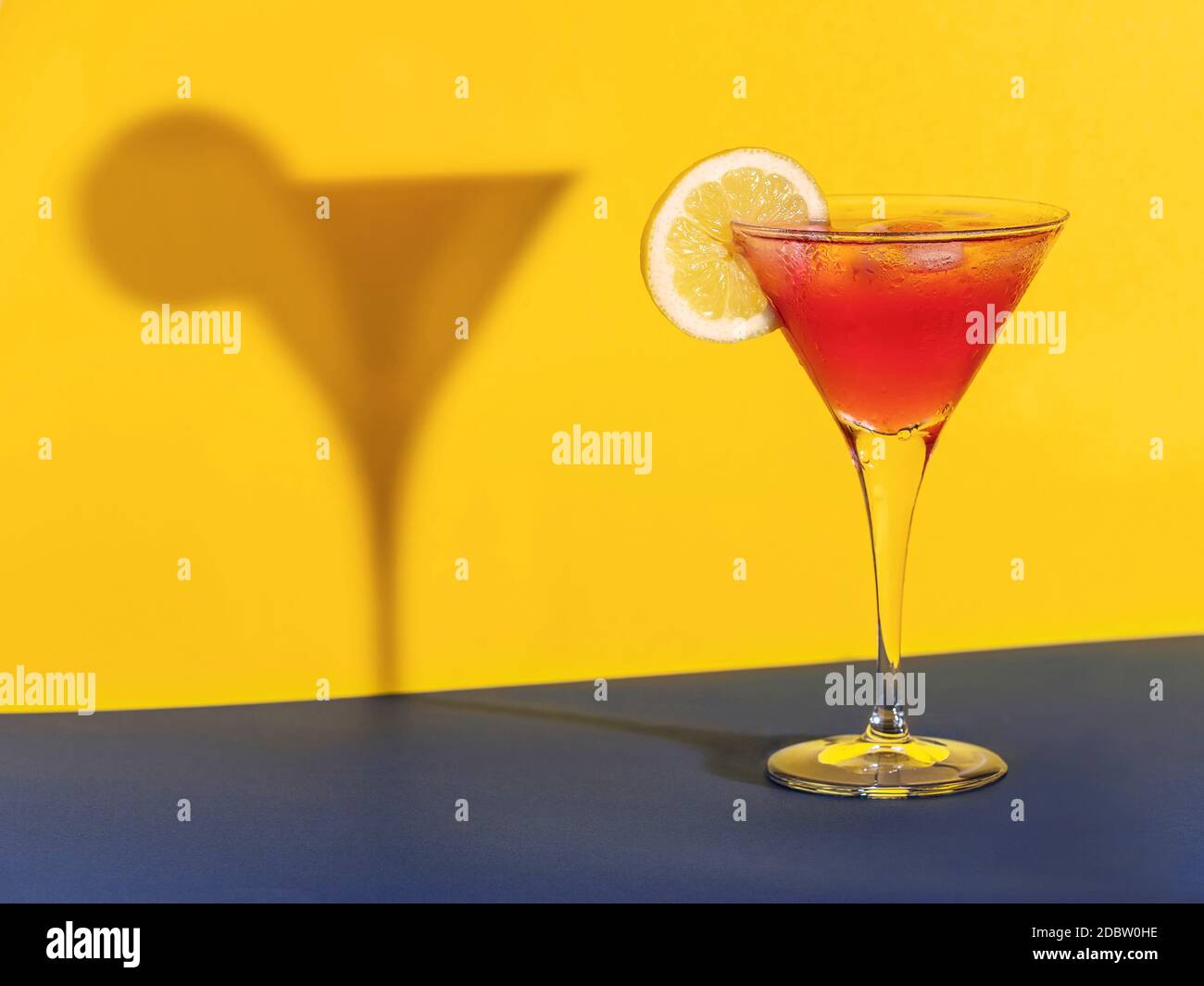 Red cocktail in a glass shaping its shadow with a lemon slice on a blue ...