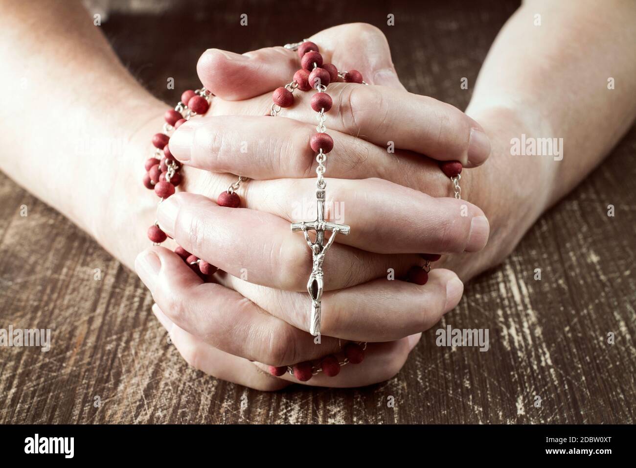 Praying hands holding red rosary with cross Stock Photo - Alamy