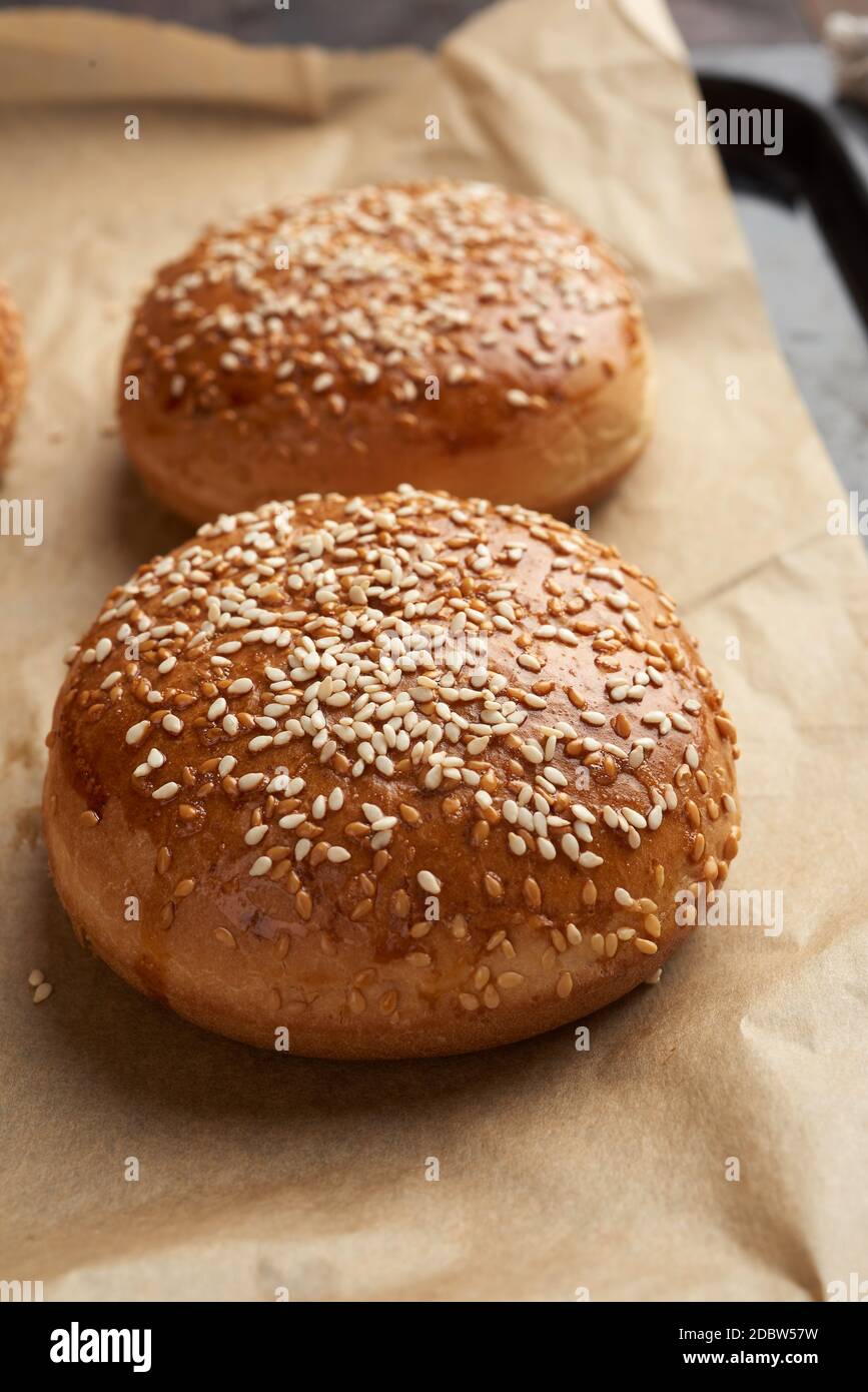 baked sesame buns on brown parchment paper, ingredient for a hamburger ...