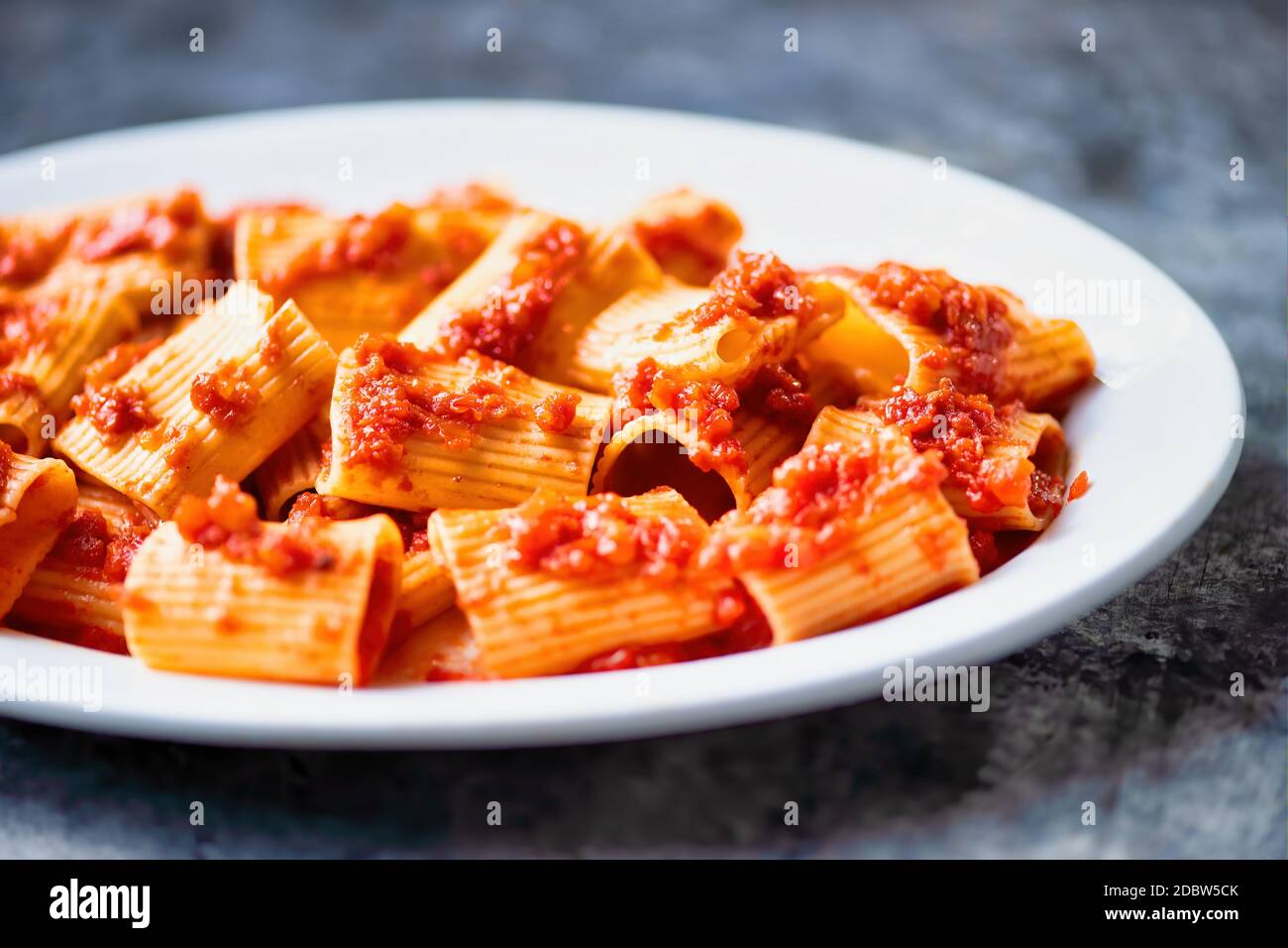 close up of a plate of rustic italian paccheri pasta in tomato sauce ...