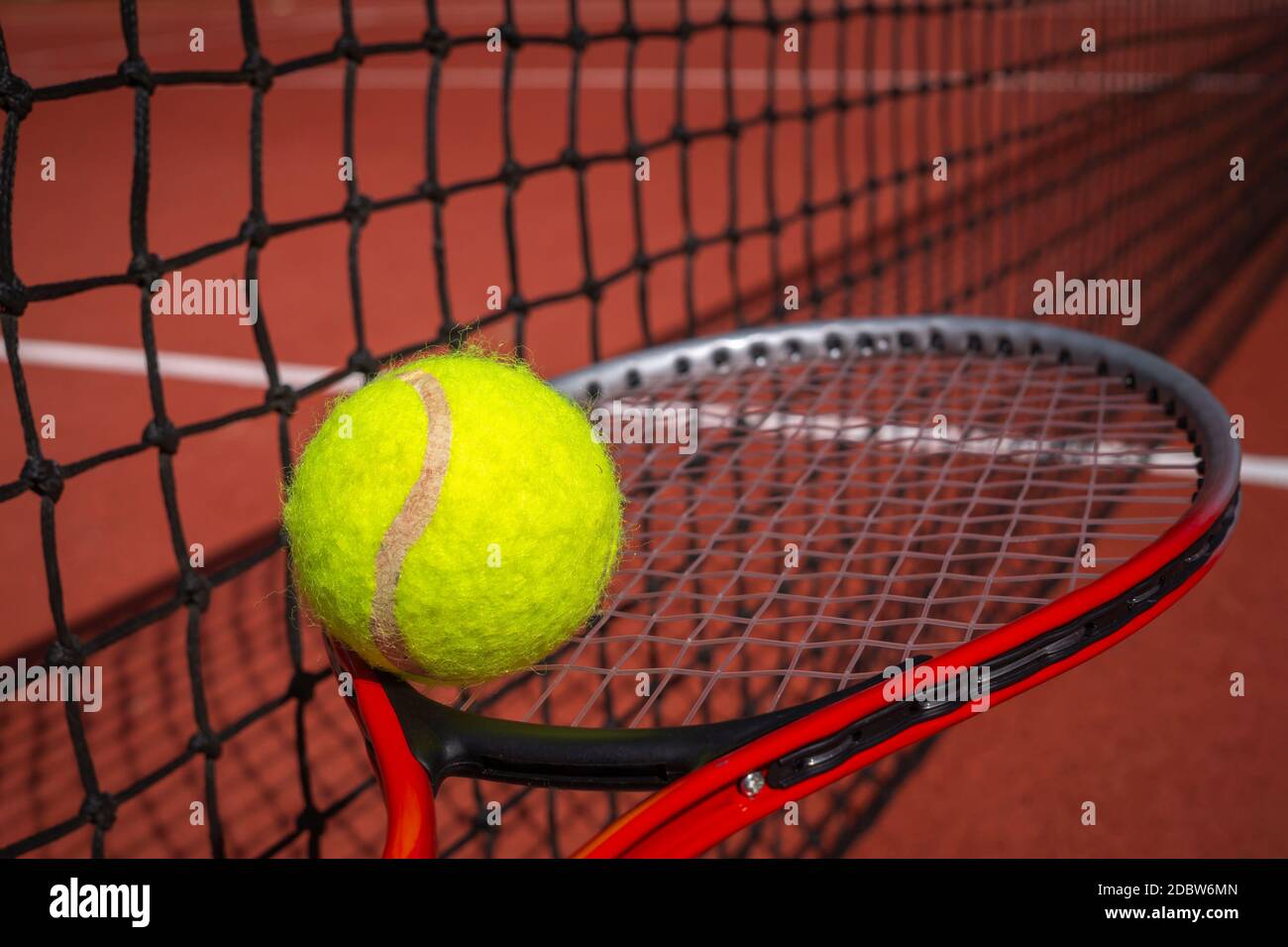 Tennis balancing ball on a racket alongside a net on a court in a sport ...