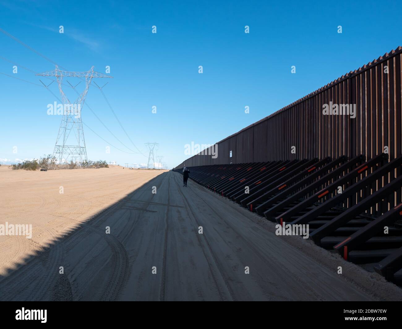 Woman walking along USA and Mexico border wall with diagonal shadow ...