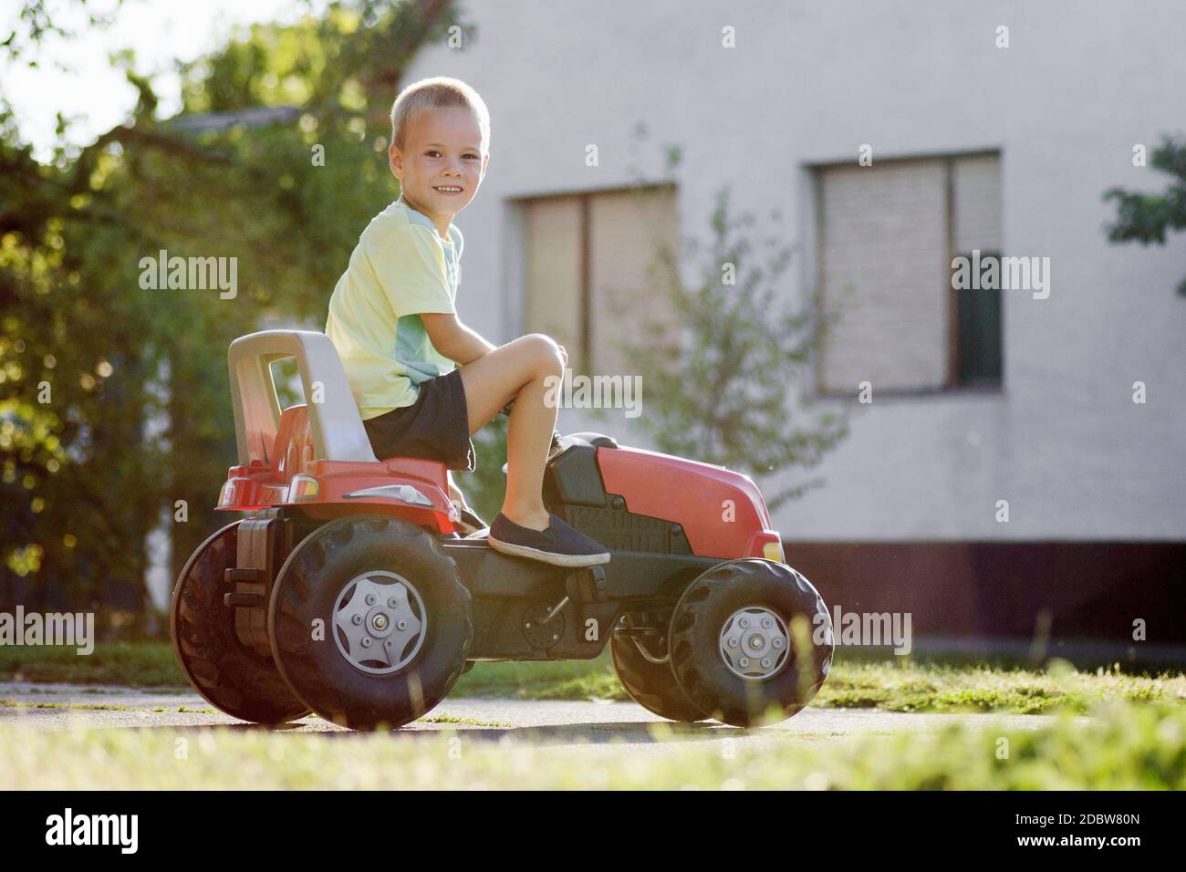 The little boy is playing driving tractor toy at the street outdoors ...