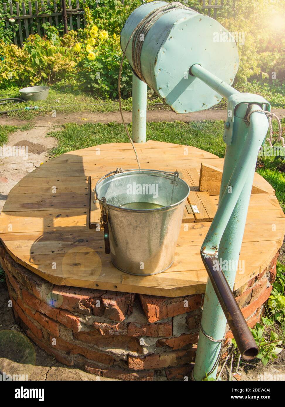 Metal bucket on a wooden lid of a brick well, open on a Sunny summer ...