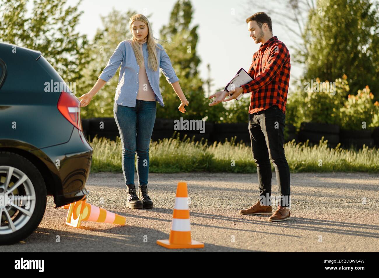 Male instructor and woman at the car and downed cone, lesson in driving ...