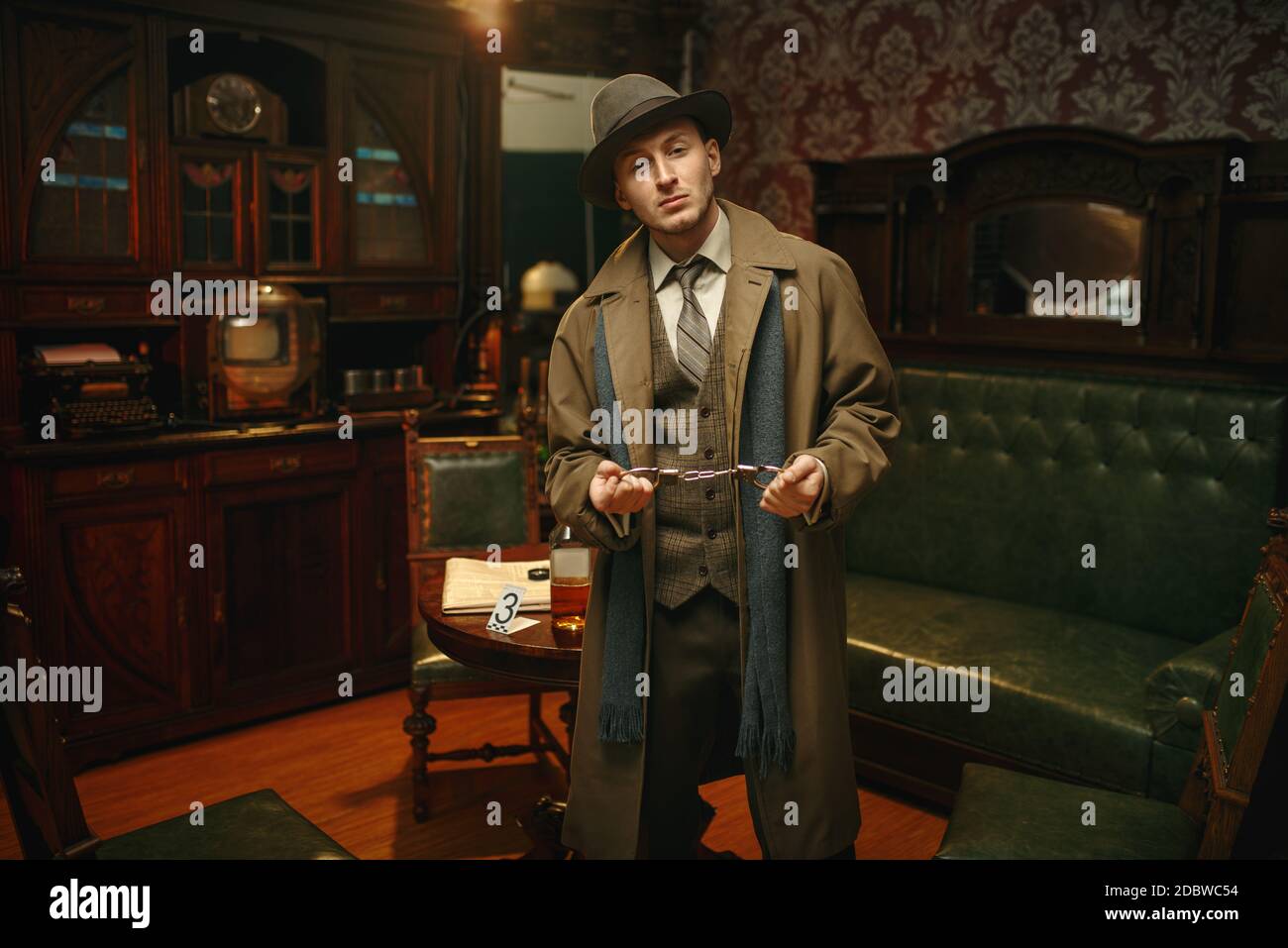 Male detective in hat and coat holds handcuffs at the crime scene ...