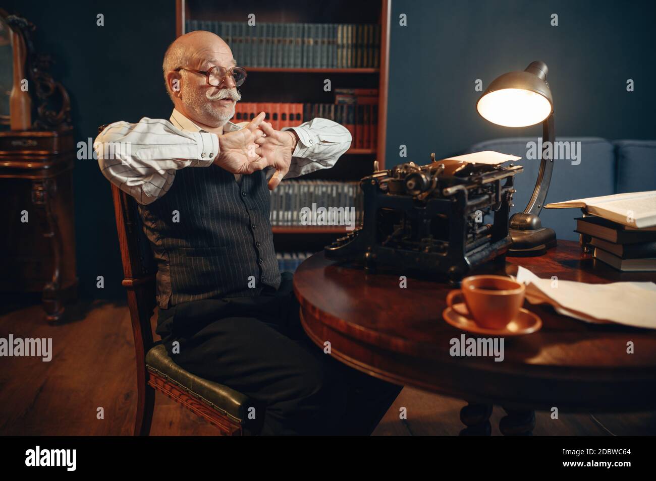 Elderly writer prepares to work on vintage typewriter in home office ...