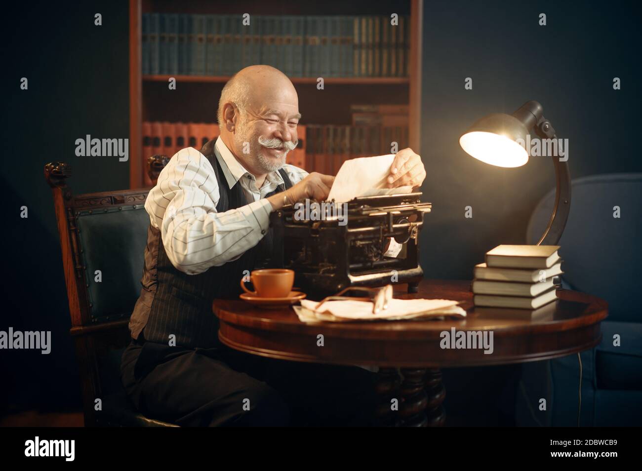 Smiling elderly writer works on retro typewriter in home office. Old ...