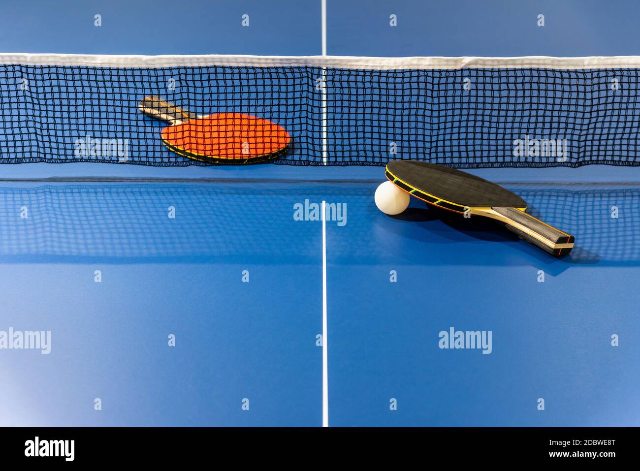 Black and red table tennis racket and a white ball on the blue ping ...