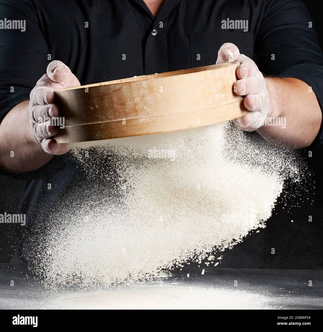 chef a man in a black uniform holds a round wooden sieve in his hands ...