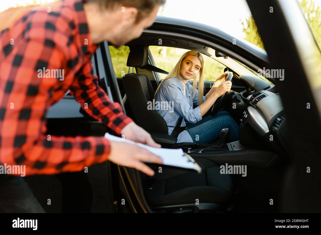 Woman in car looks on instructor with checklist, driving school. Man ...
