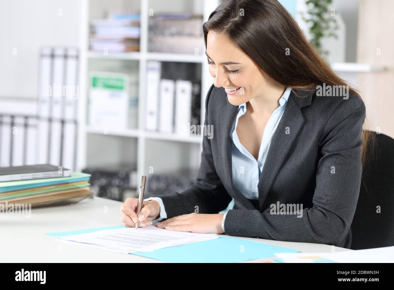 Happy executive woman signs contract sitting on a desk at the office ...