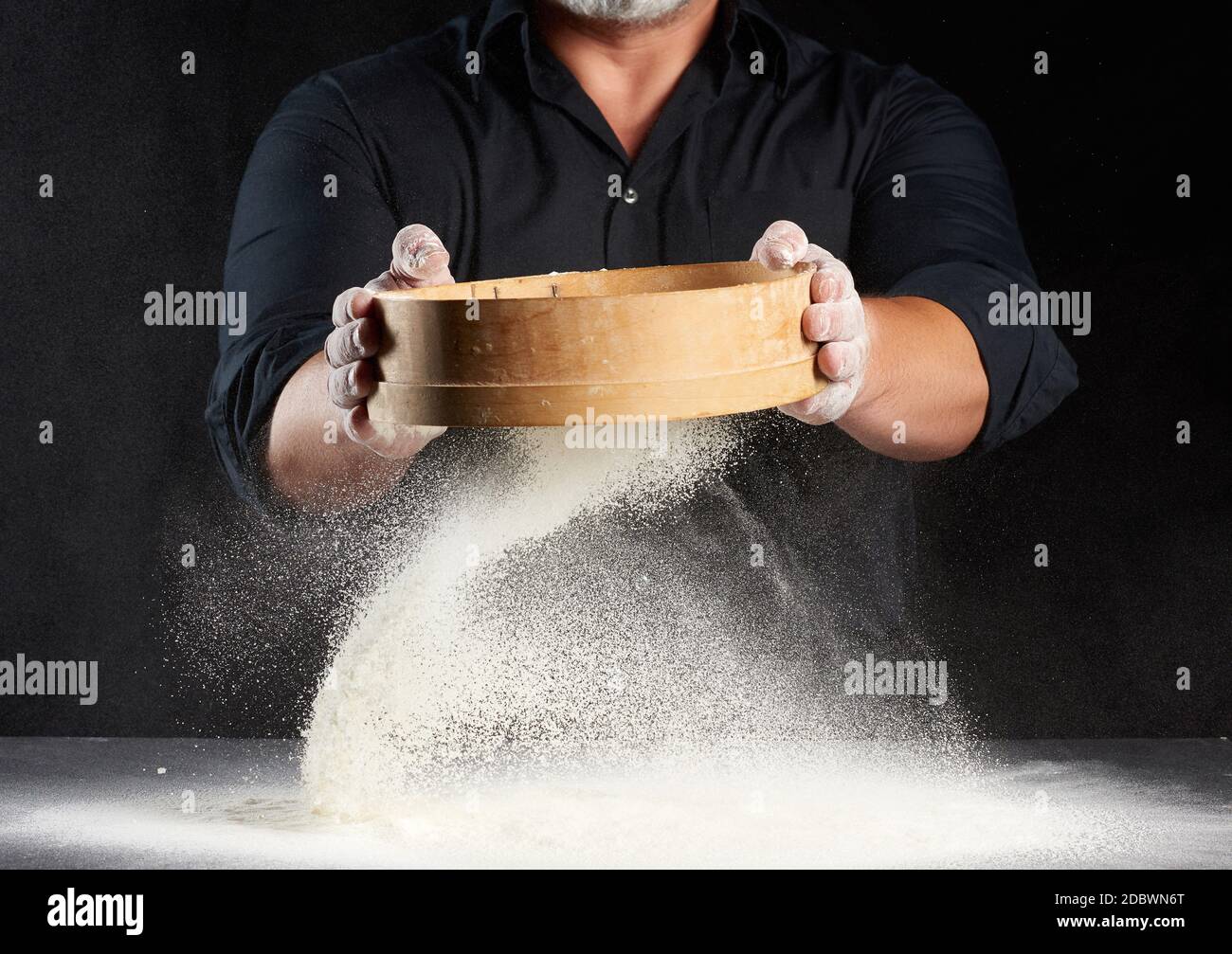 chef a man in a black uniform holds a round wooden sieve in his hands ...