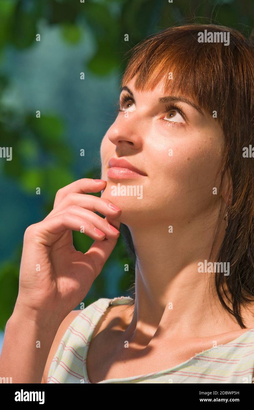 Partial head portrait of a young woman looking up, thoughtfully holding ...