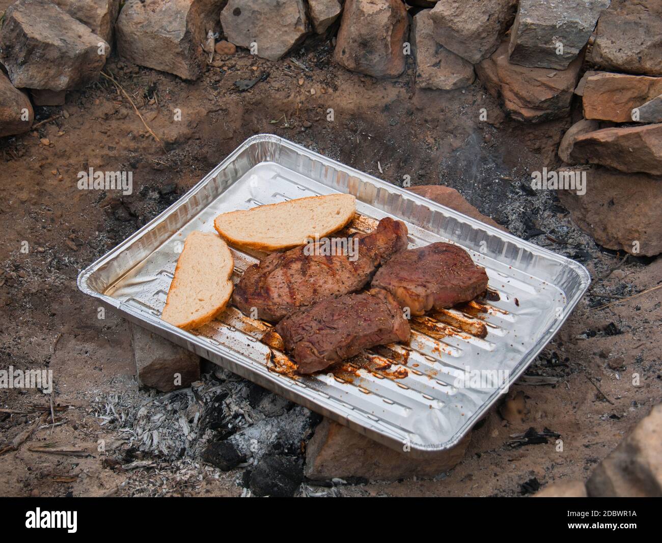 Three steaks and two slices of bread are grilled in an aluminium dish ...