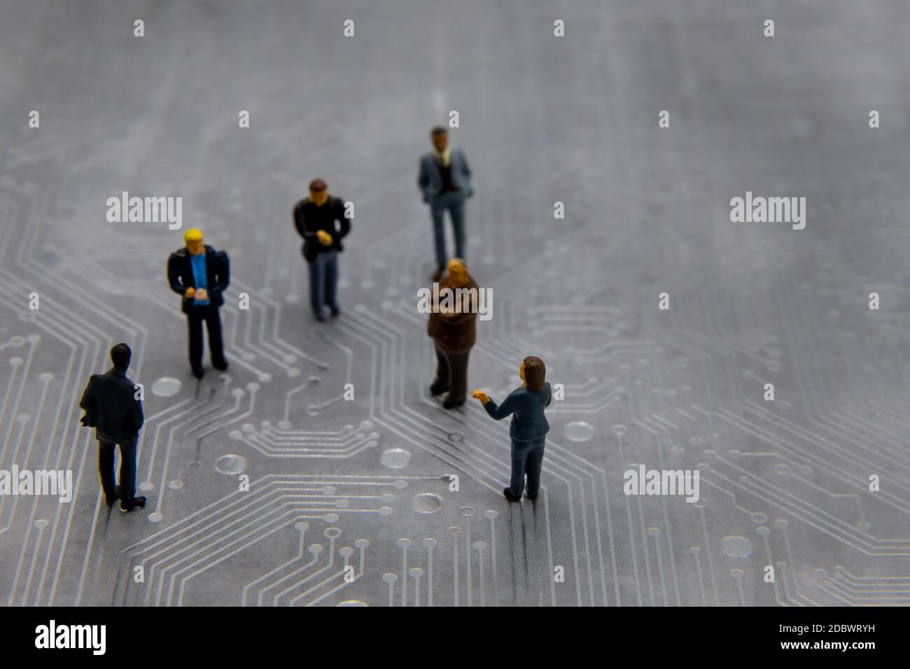 Miniature figurines posed as business people in a meeting over abstract ...