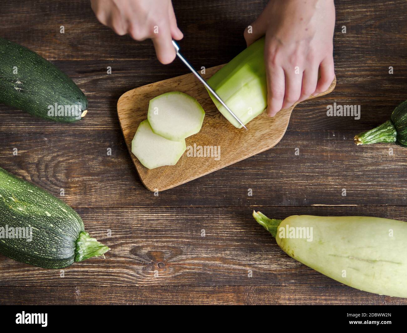 Zucchini harvest. Woman slices zucchini on wooden table. Farm organic ...