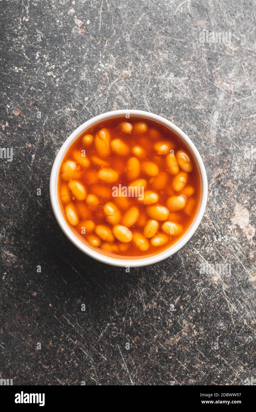 Baked beans in bowl. Beans with tomato sauce on kitchen table. Top view ...