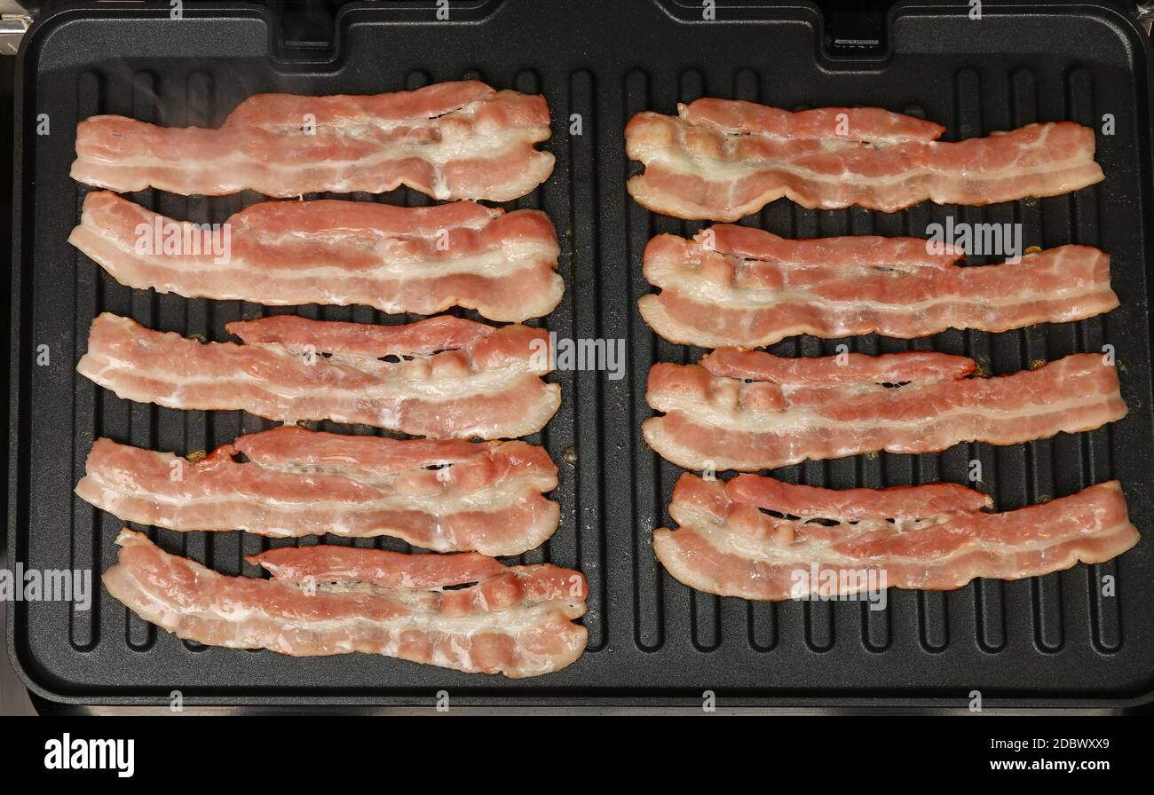 Close up cooking several bacon slices, rashers, on electric grill ...