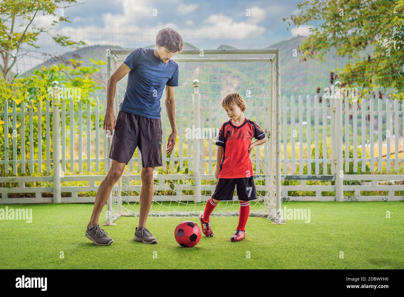 Little cute kid boy in red football uniform and his trainer or father ...
