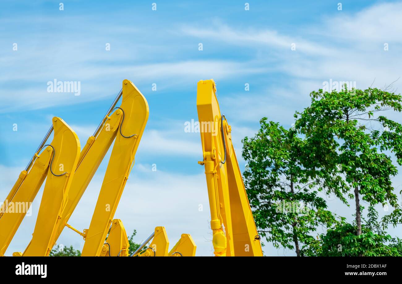 Selective focus on hydraulic piston arm of yellow backhoe on blur tree ...