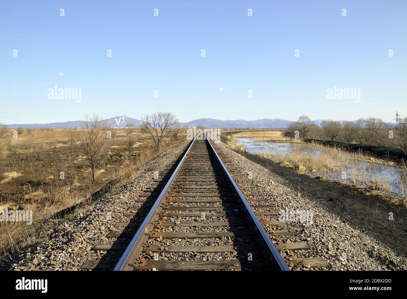 Railroad and depressive landscape with dry grass, swamp and blue sky ...