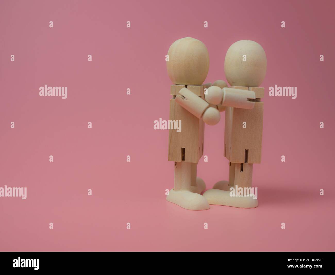 2 wooden dolls hugging each other on a pink background. Concept of ...