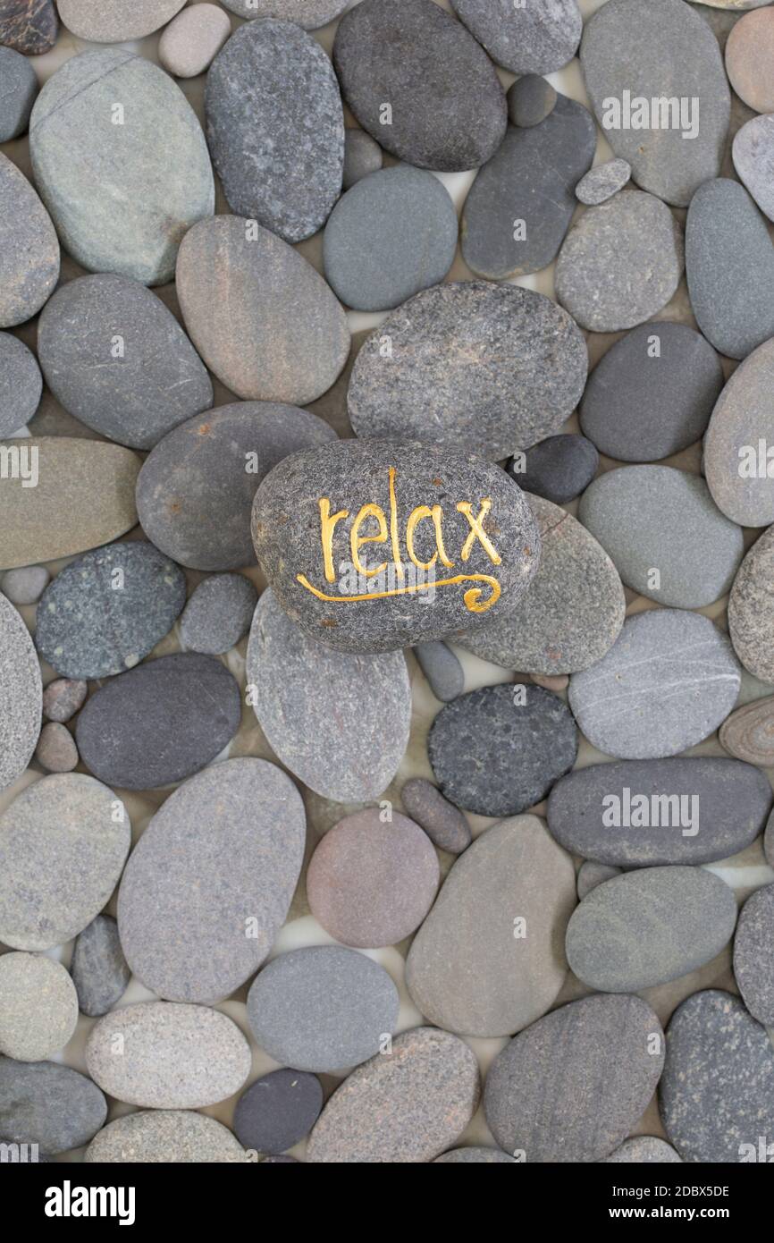 smooth grey pebble with handwritten word relax in golden letters ...