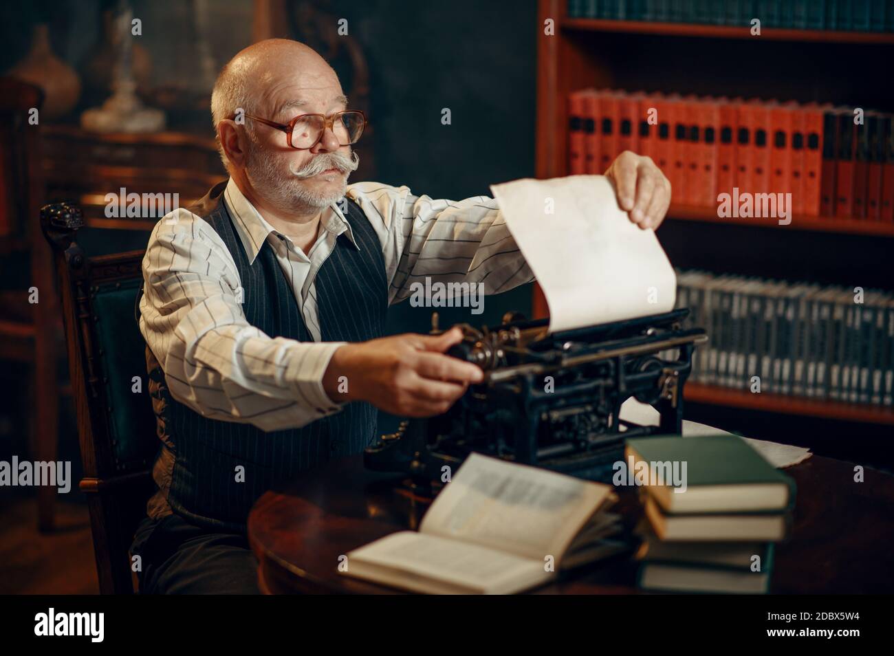 Elderly writer inserts paper into the vintage typewriter in his home ...