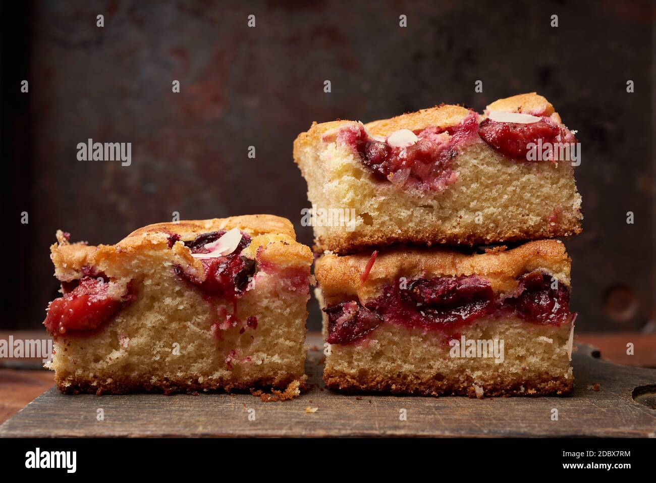 stack of square baked sponge cake slices with plums on wooden kitchen ...