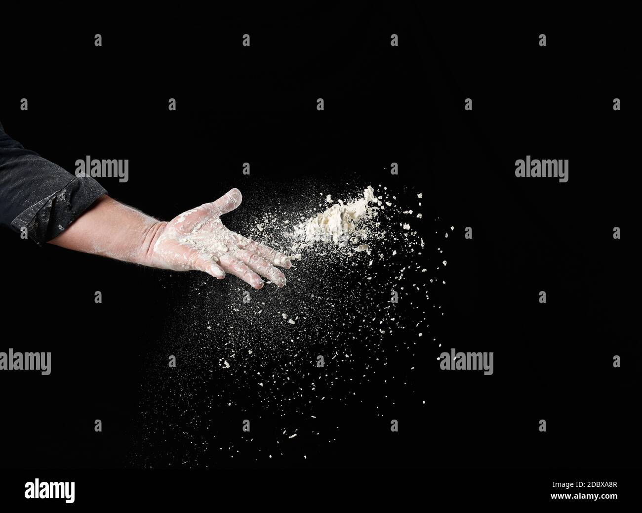 baker's male hand throws up a handful of white wheat flour on a black ...