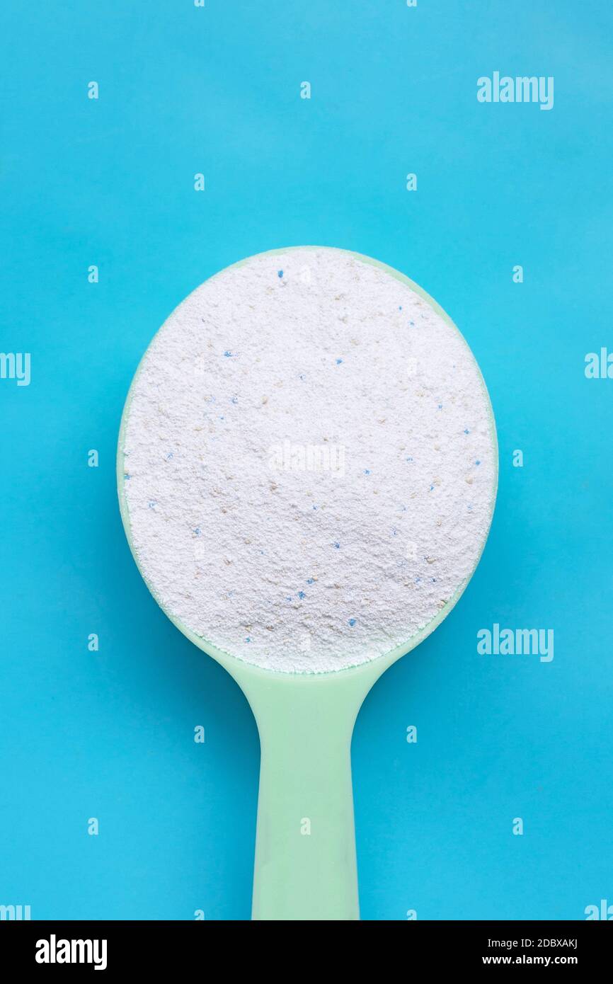 Detergent powder in measuring spoon on blue background. Laundry concept ...