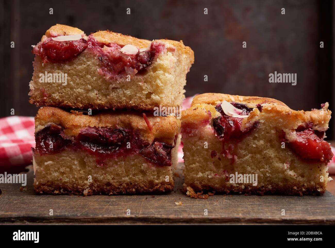 stack of square baked sponge cake slices with plums on wooden kitchen ...