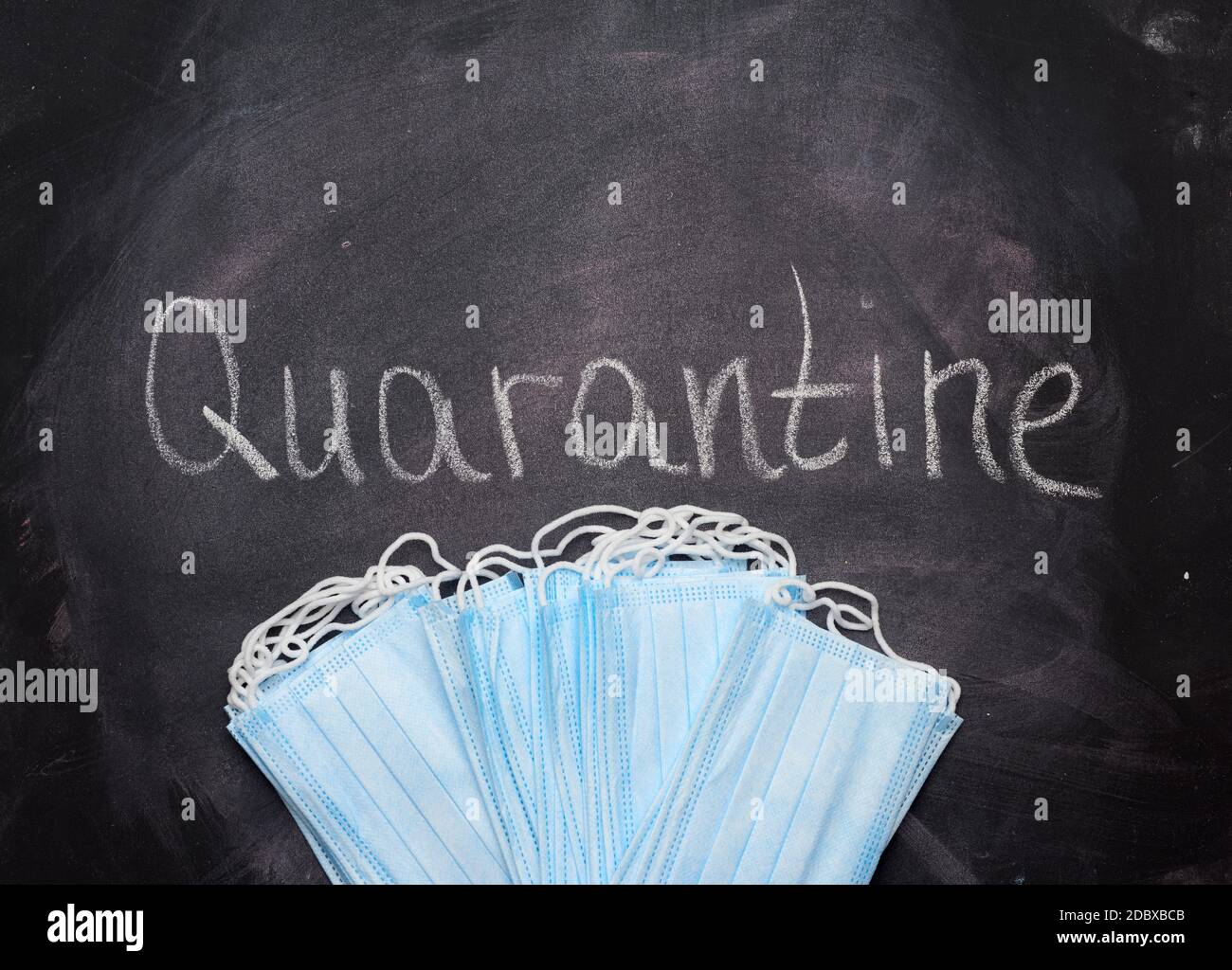 disposable medical face mask and quarantine lettering on black chalk ...