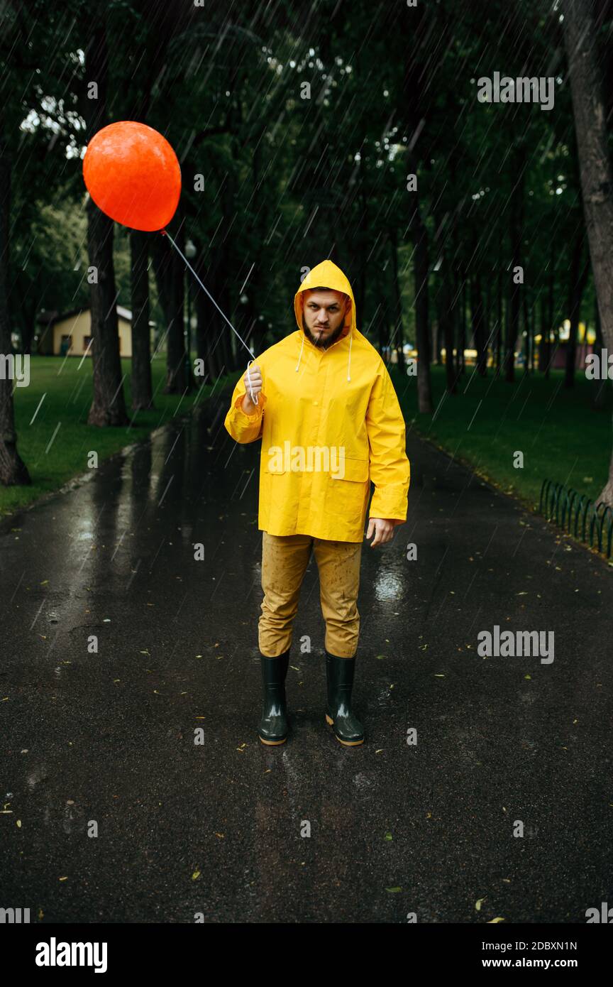 Sad man with balloon walking in summer park in rainy day. Male person ...