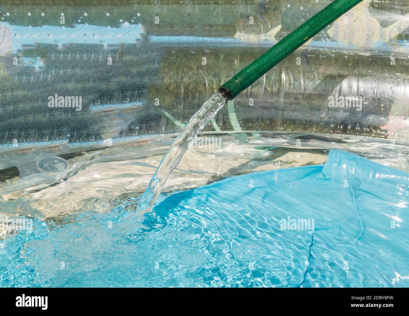 Green plastic hose close up with spilling water into outdoor pool on ...