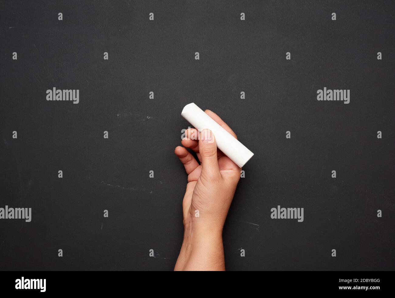 hand holds a piece of white chalk on the background of an empty black ...