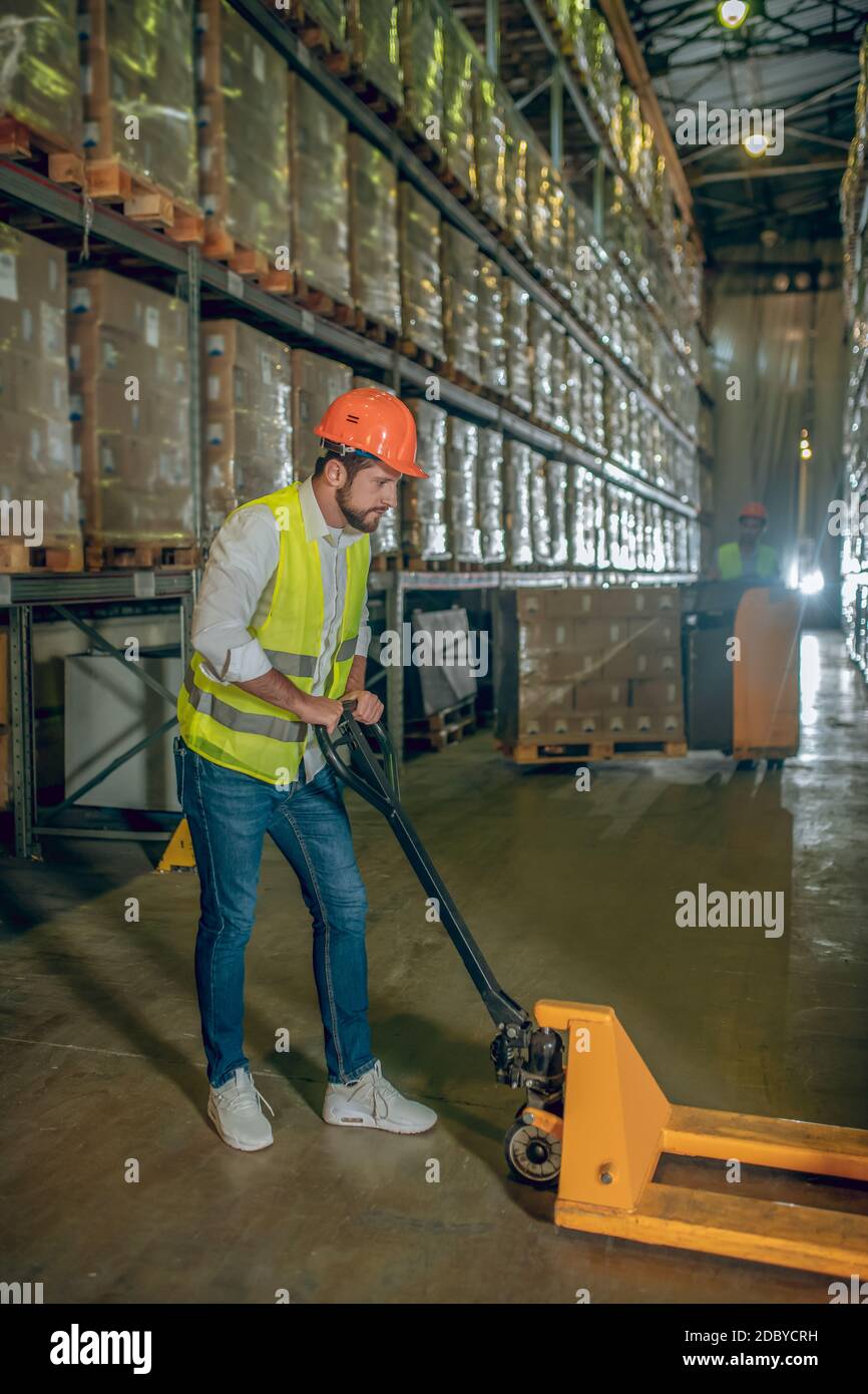 Worker in a vest and helmet standing near the loader Stock Photo - Alamy