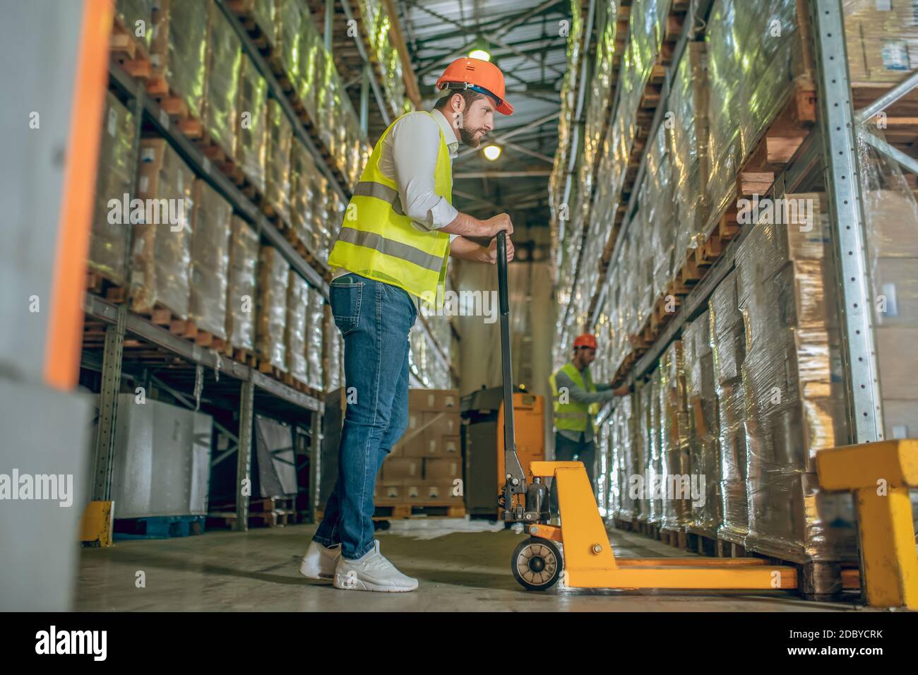 Worker in a yellow vest and helmet standing near the loader Stock Photo ...